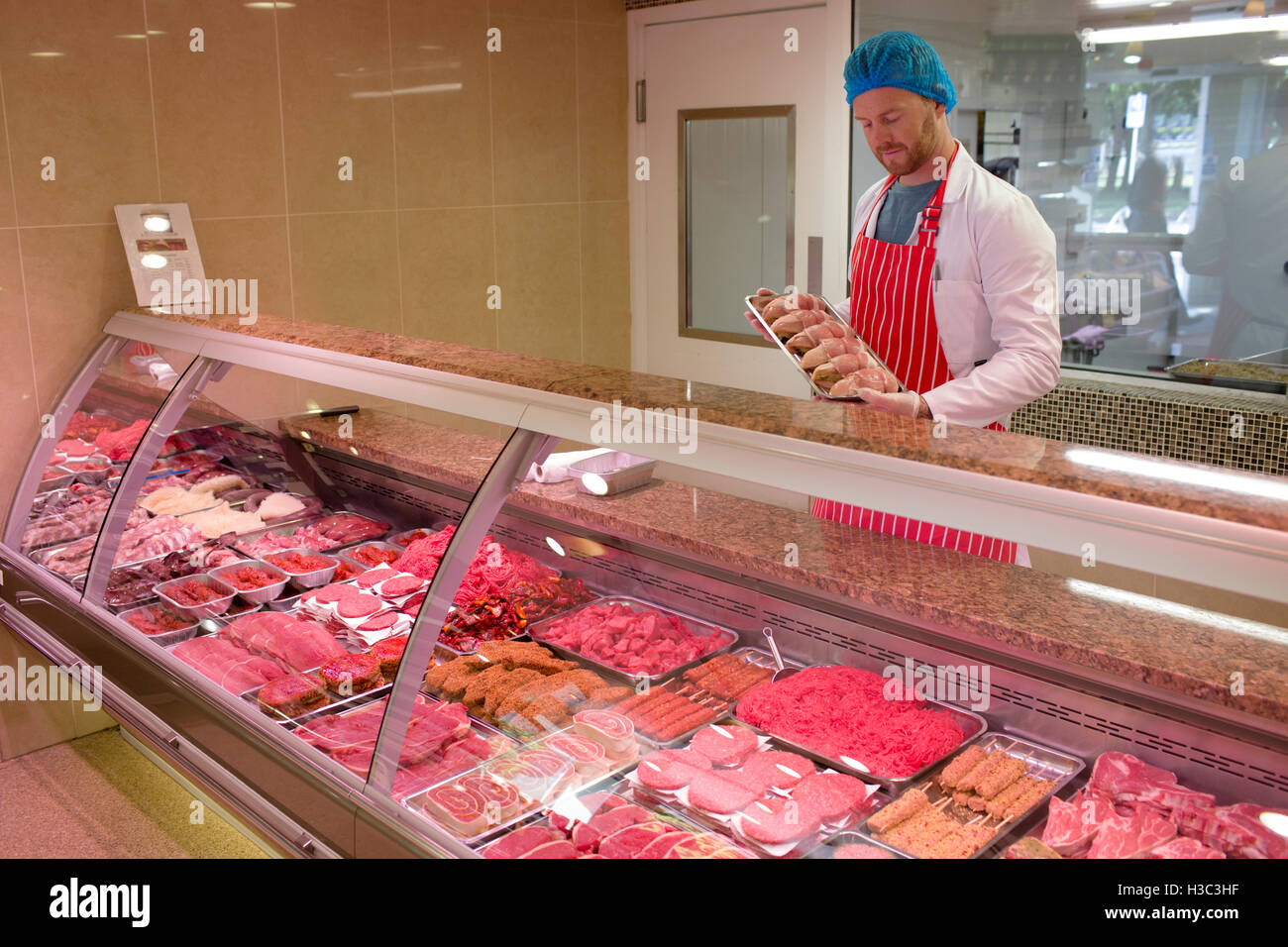 Butcher standing at meat counter Stock Photo - Alamy