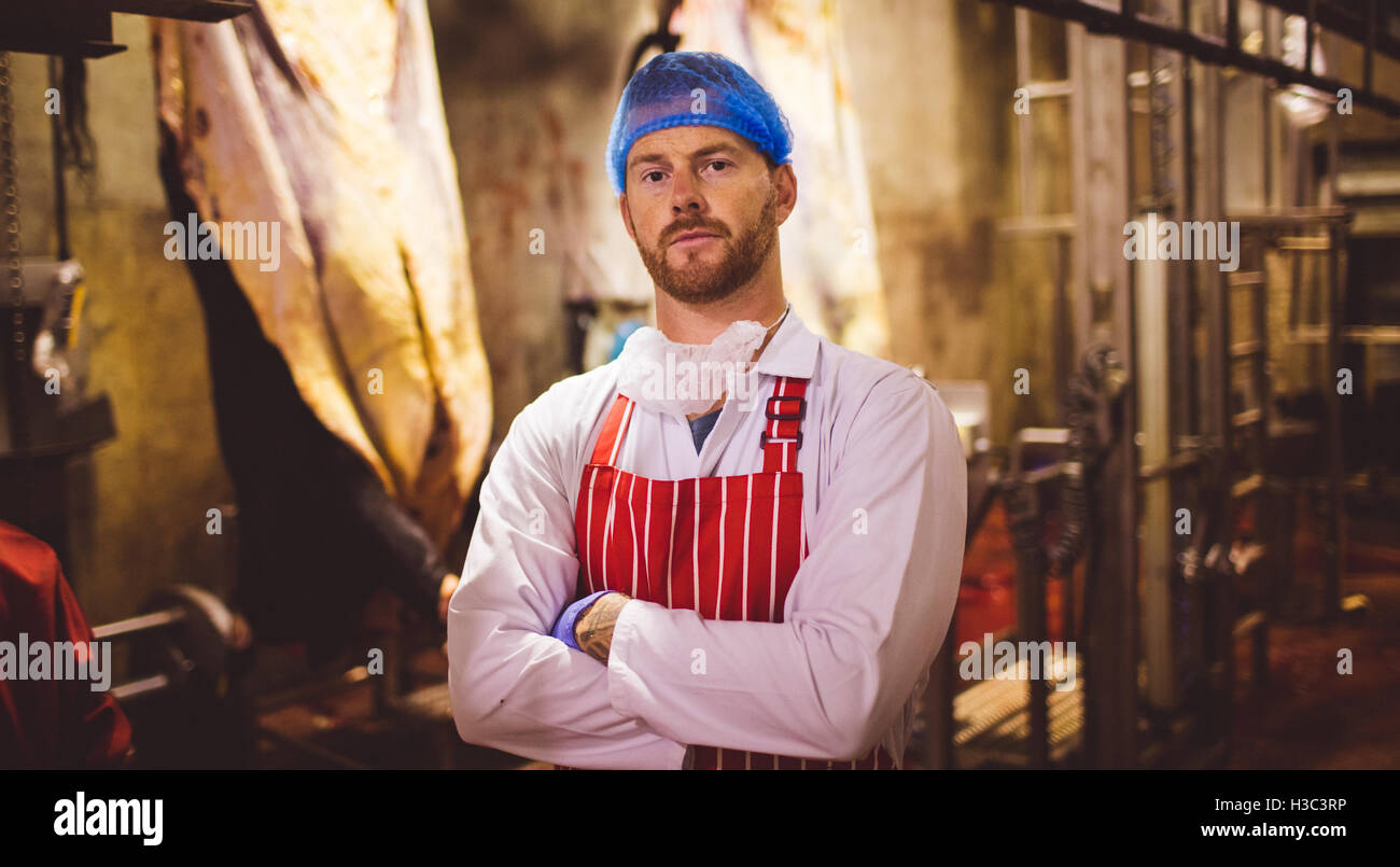 Portrait of butcher standing with arms crossed in meat storage room ...