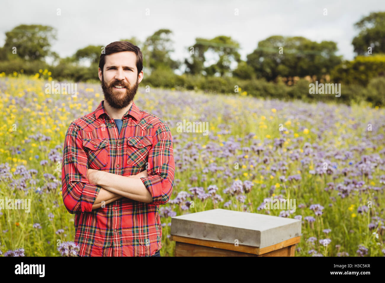 Beekeeper standing with arms crossed in flower field Stock Photo - Alamy
