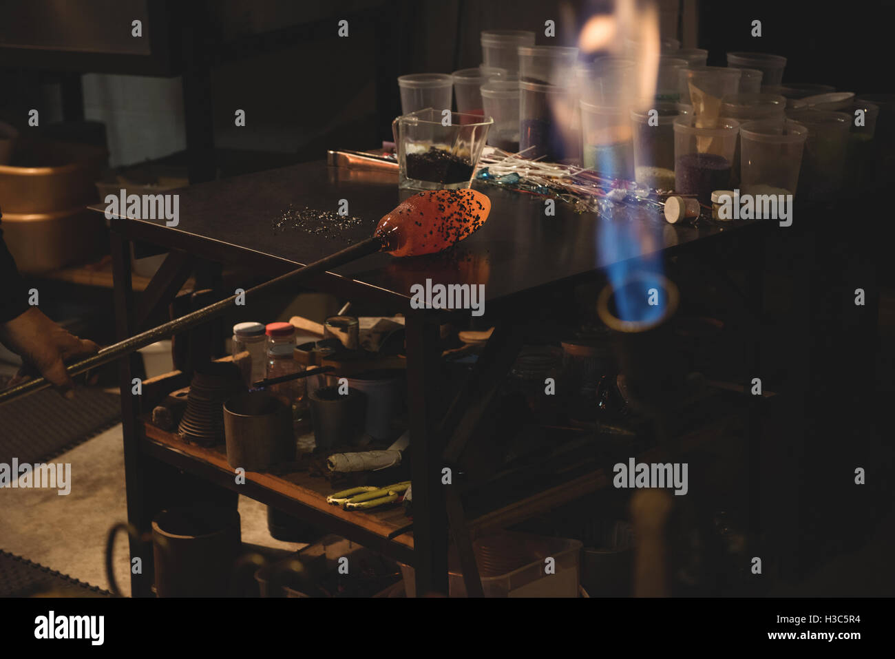 Glassblower rolling molten glass over frit glass on a marver table ...