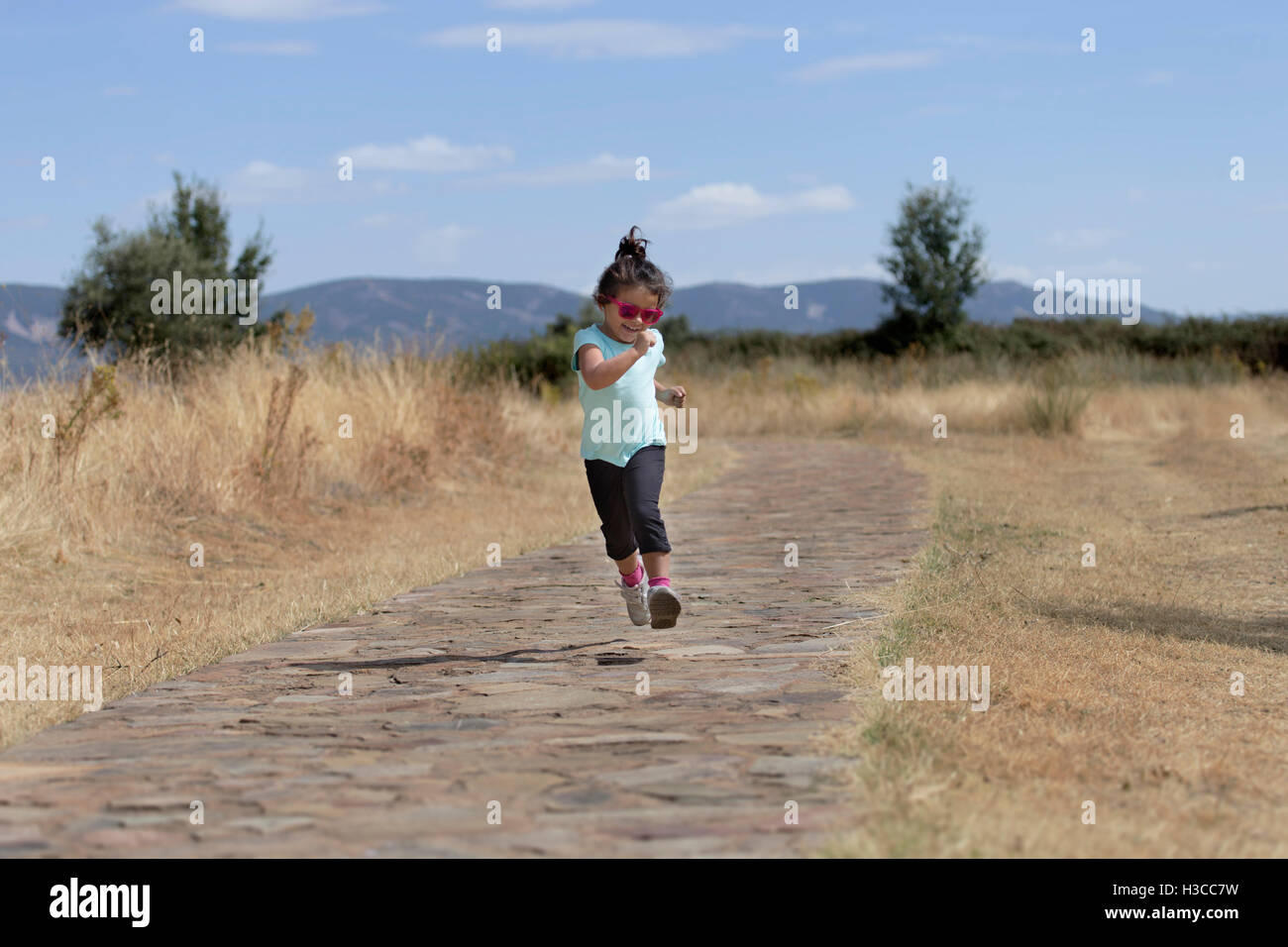 Portrait of pretty little girl running down the footpath in a sunny day ...