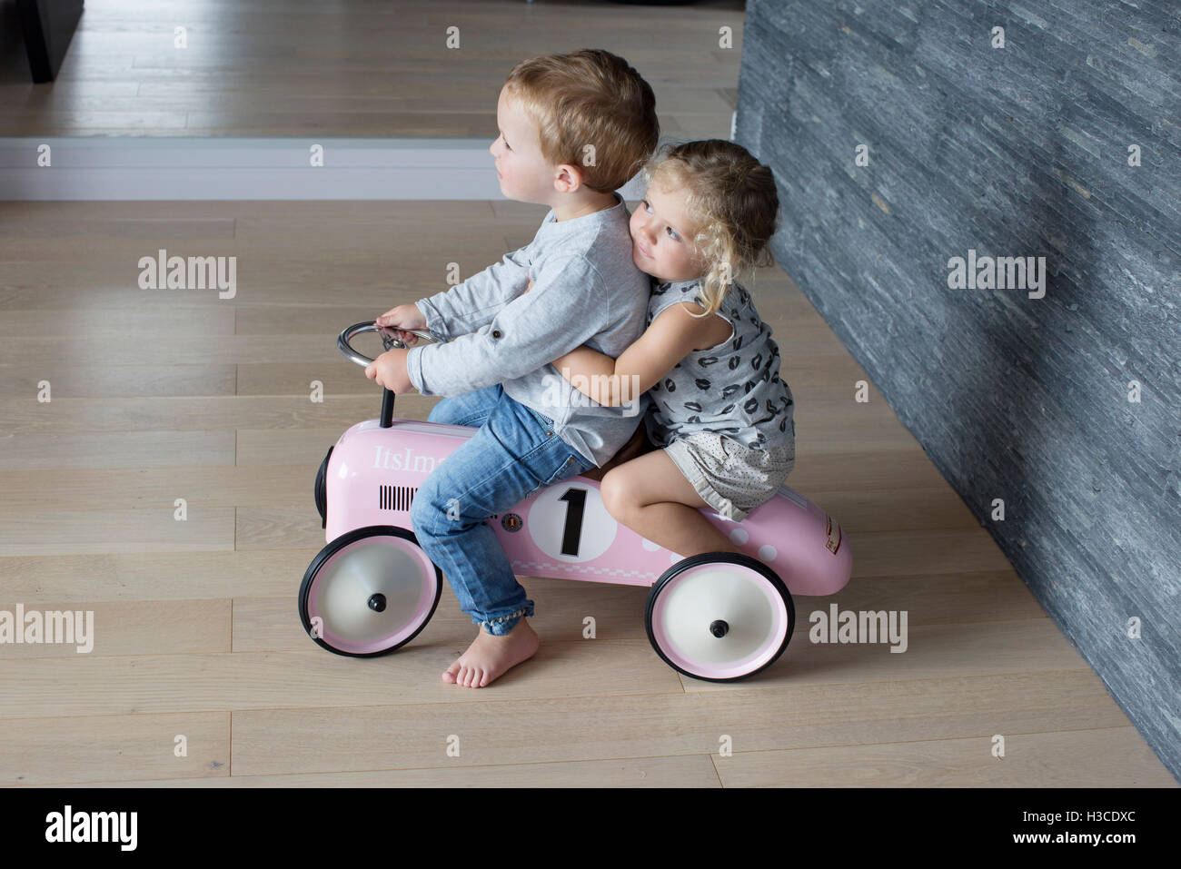 Young siblings riding on toy car together Stock Photo - Alamy