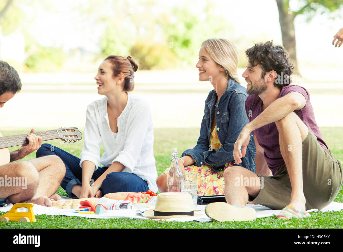 Firends listening to man playing guitar while picnicking in park Stock ...