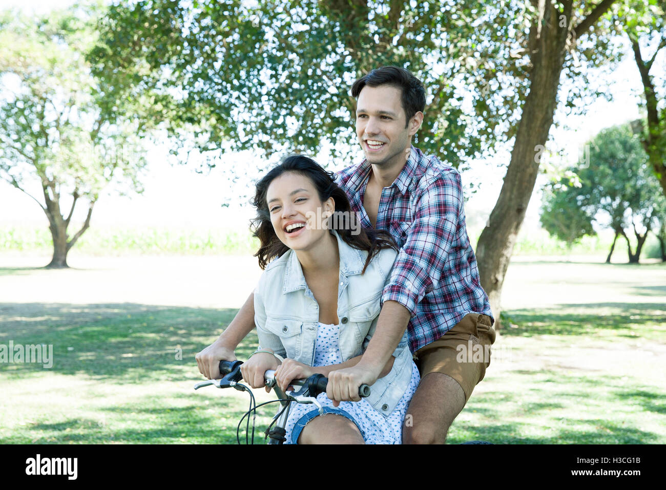 Young couple riding bicycle together with girlfriend seated sidesaddle ...