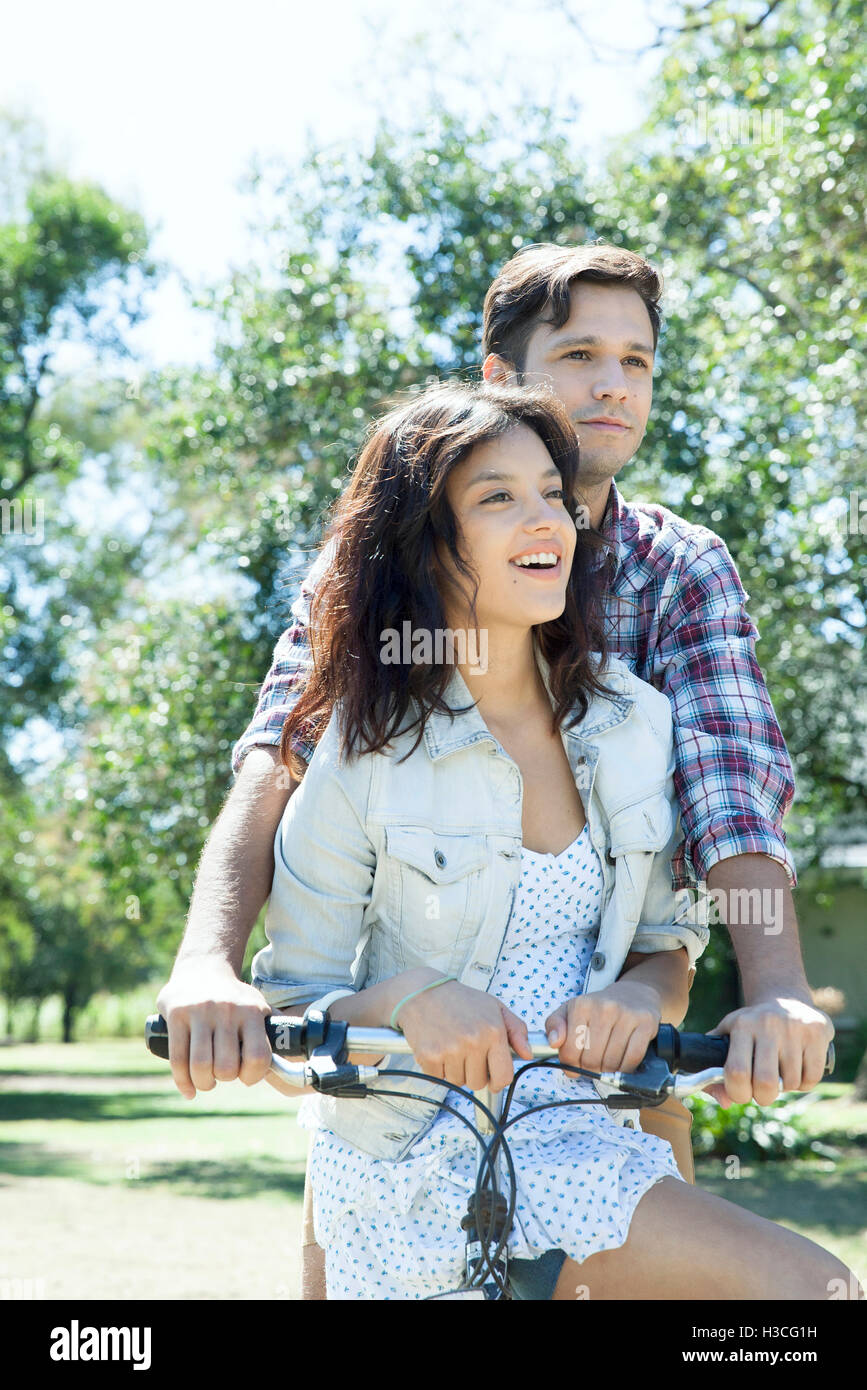 Young couple riding bicycle together with girlfriend seated sidesaddle ...