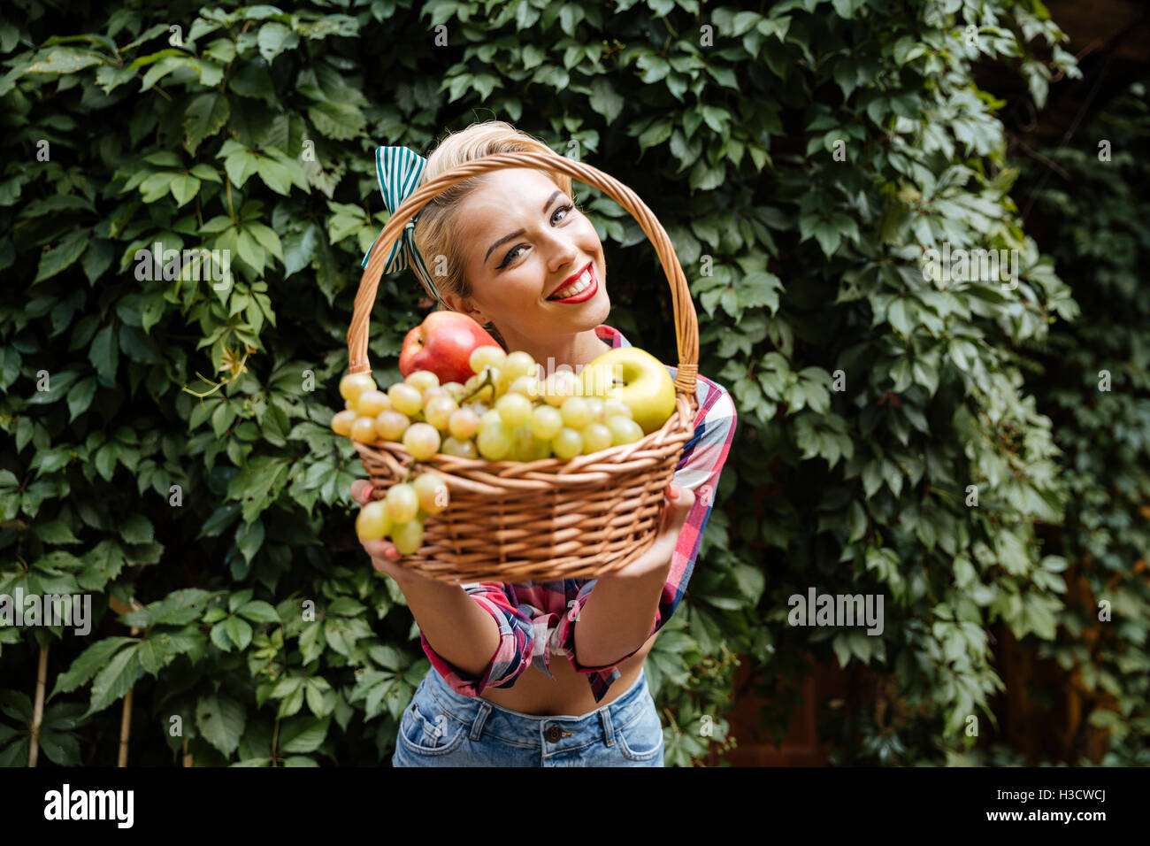 Smiling lovely pin-up girl standing and giving you basket of fresh ...