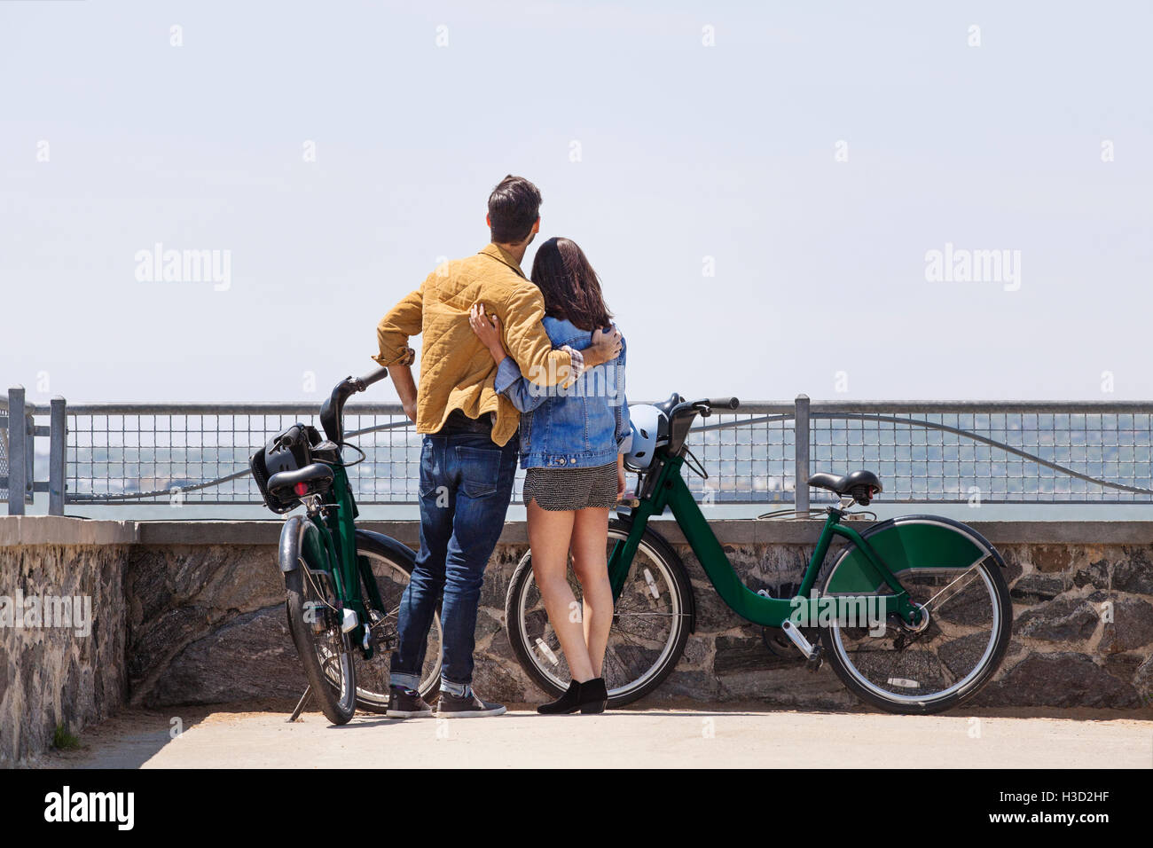 Rear view of couple standing with arms around at observation point ...