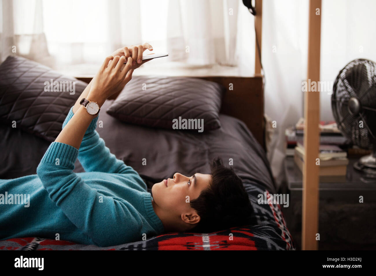 Side view of man using smart phone while lying on bed at home Stock ...