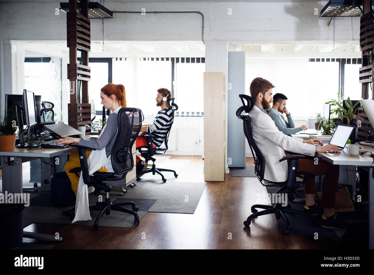 Side view of business people working at computer desks in creative ...