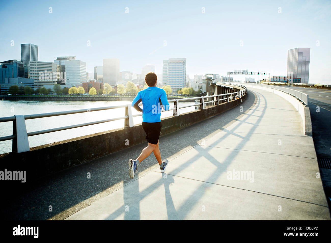 Rear view of male athlete running on bridge against clear sky Stock ...
