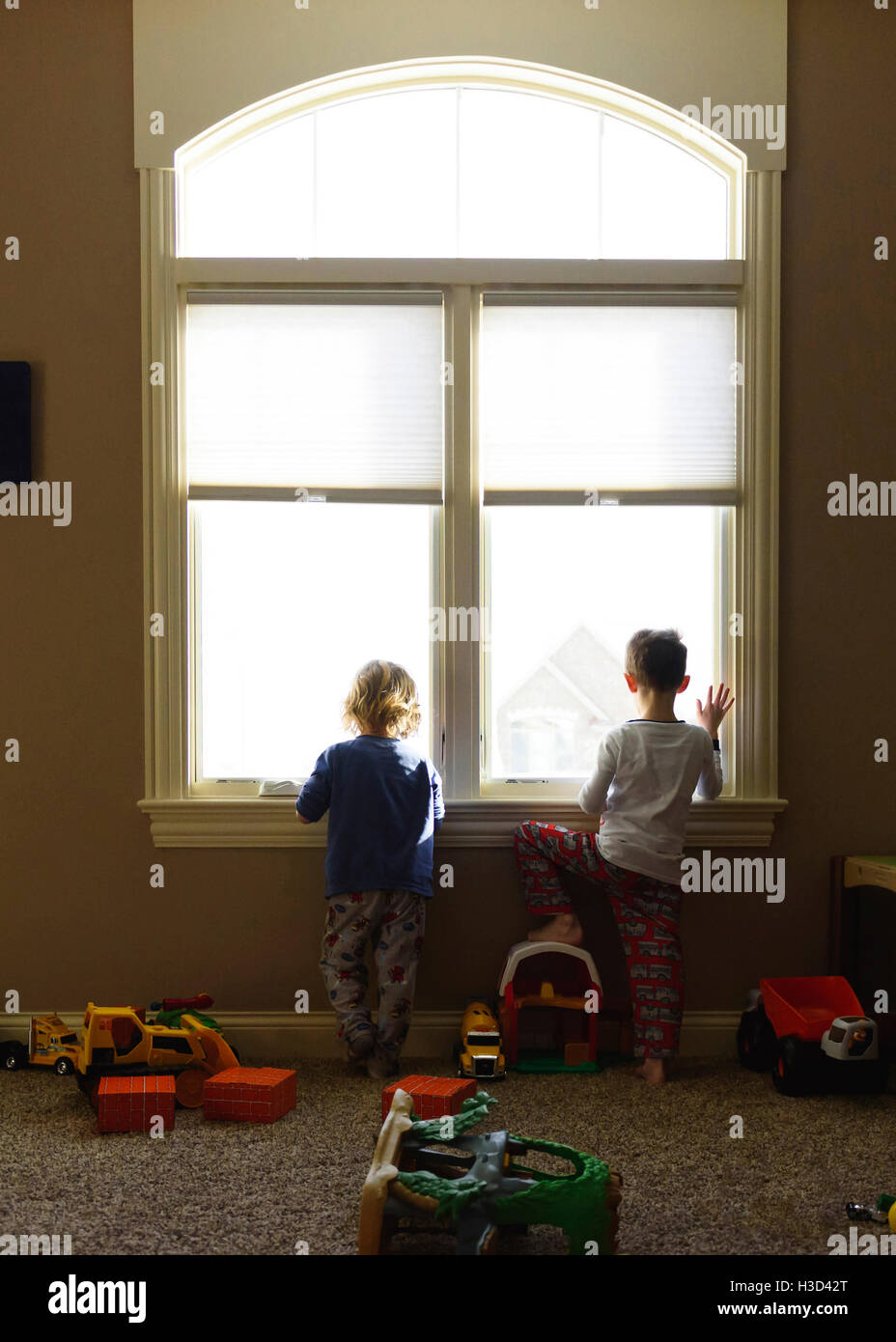 Rear view of boys looking through window at home Stock Photo - Alamy