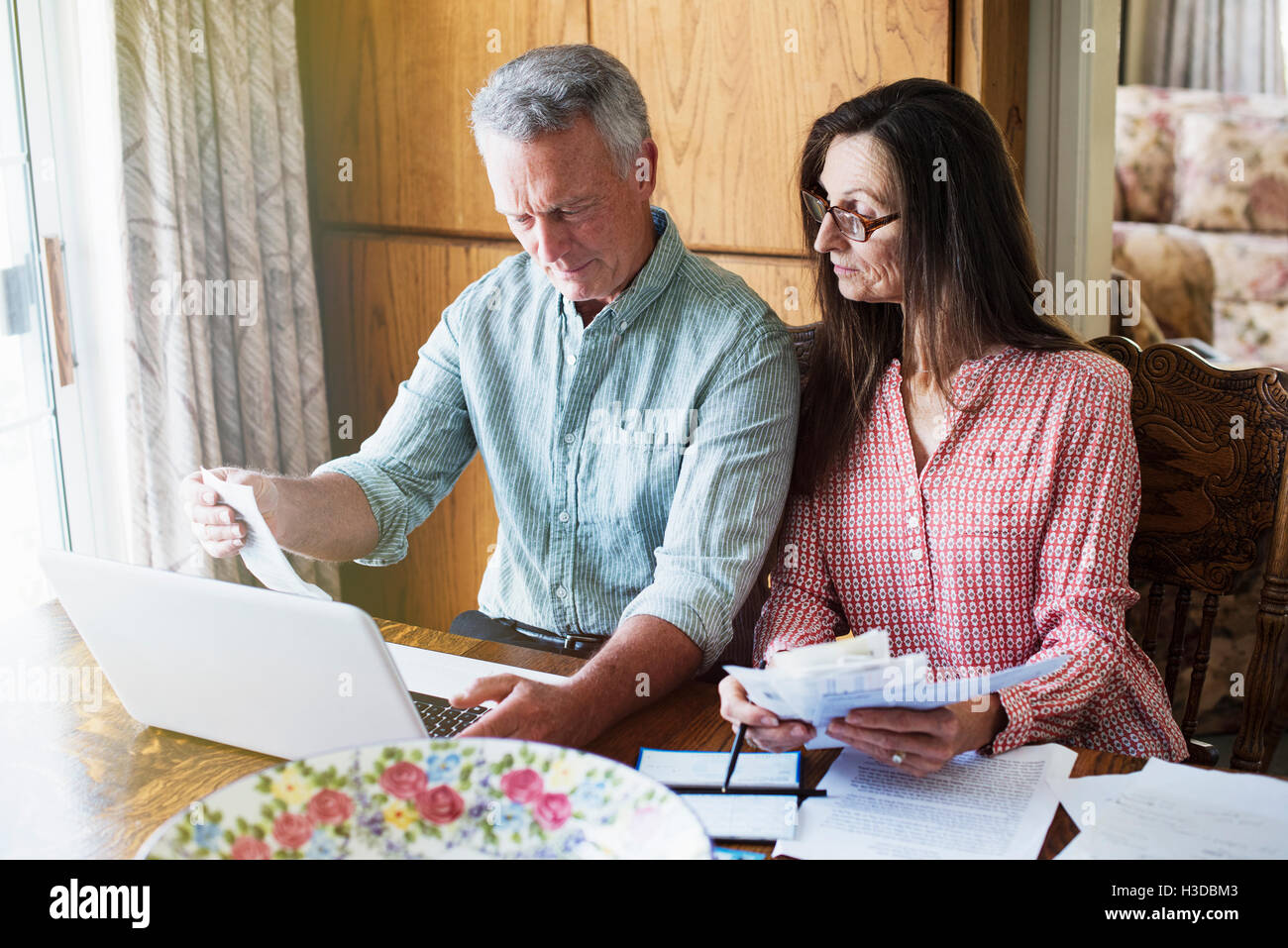 Senior couple sitting at a dining table, using a laptop computer ...