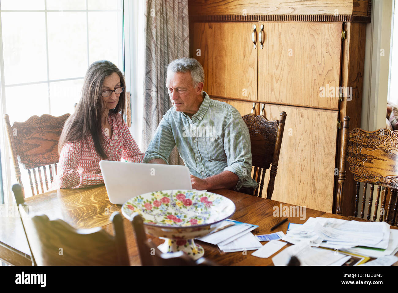 Senior couple sitting at a dining table, using a laptop computer ...