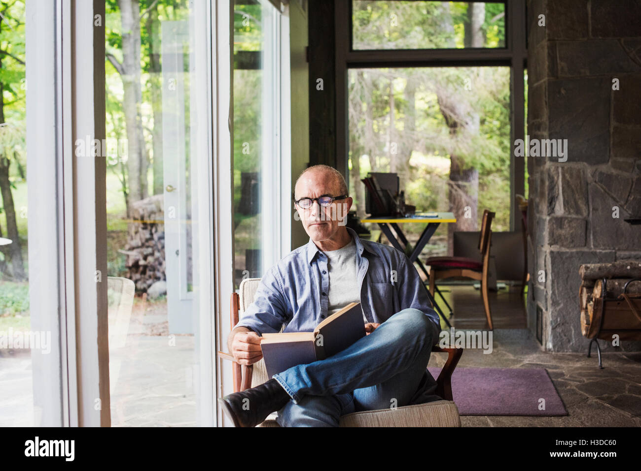 A man seated by a window reading a book Stock Photo - Alamy