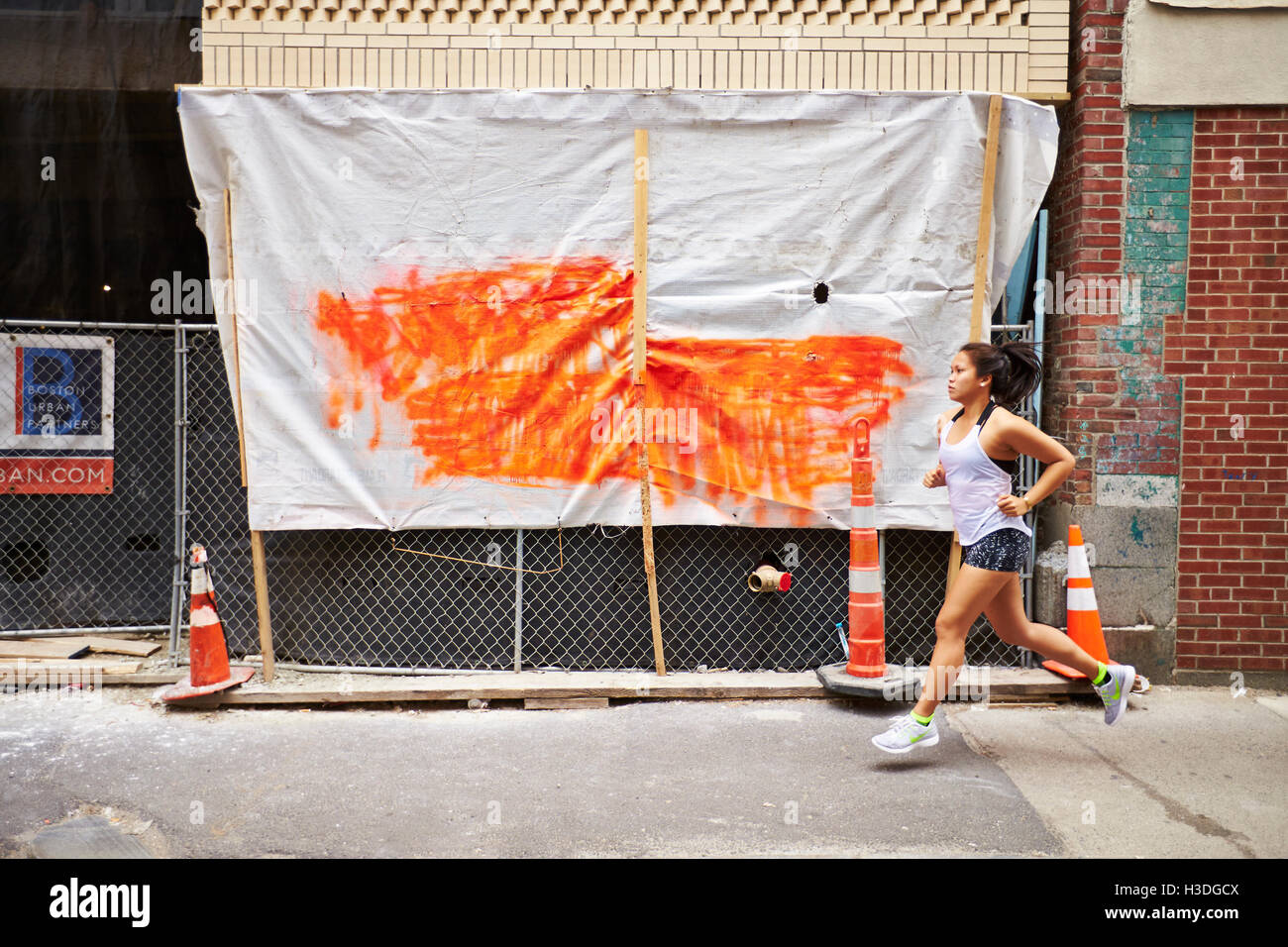 A young asian woman runs by a construction site on a city street Stock ...