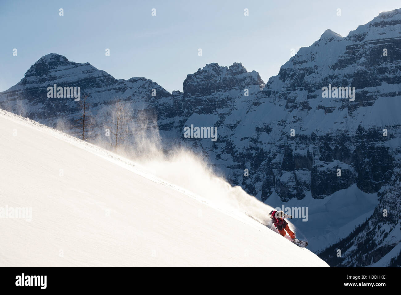 A snowboarder doing a slash against a dramatic mountain background ...