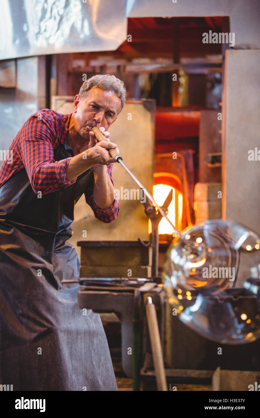 Glassblower shaping a glass on the blowpipe at glassblowing factory ...