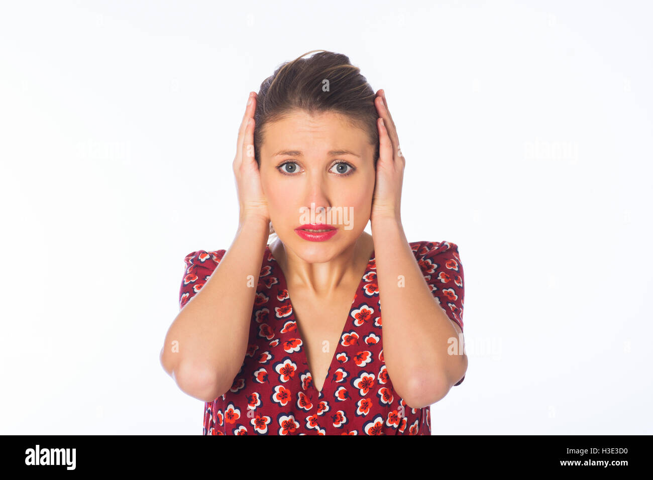Scared young woman hands on side of head against a white background ...