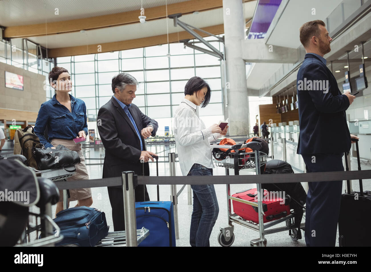 Passengers waiting in queue at a check-in counter with luggage Stock ...