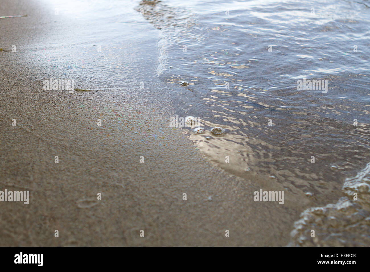 Beach with calm waves, smooth wet sand, and light reflection on water ...