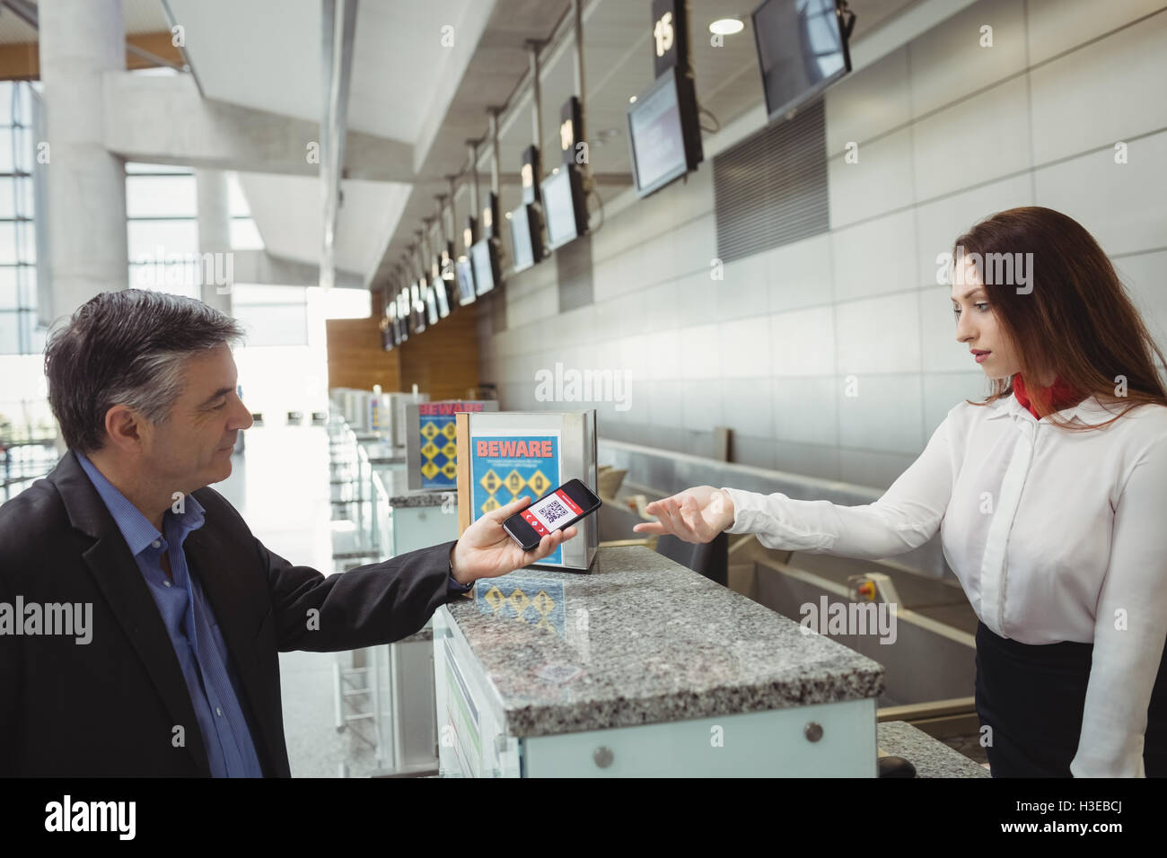 Businessman showing mobile boarding pass to airline check-in attendant ...
