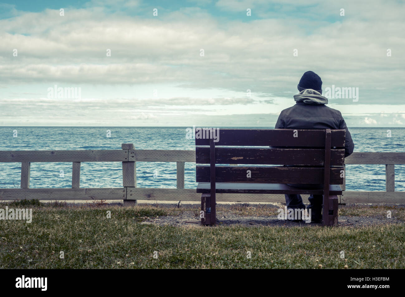Man sitting on bench overlooking sea Stock Photo - Alamy