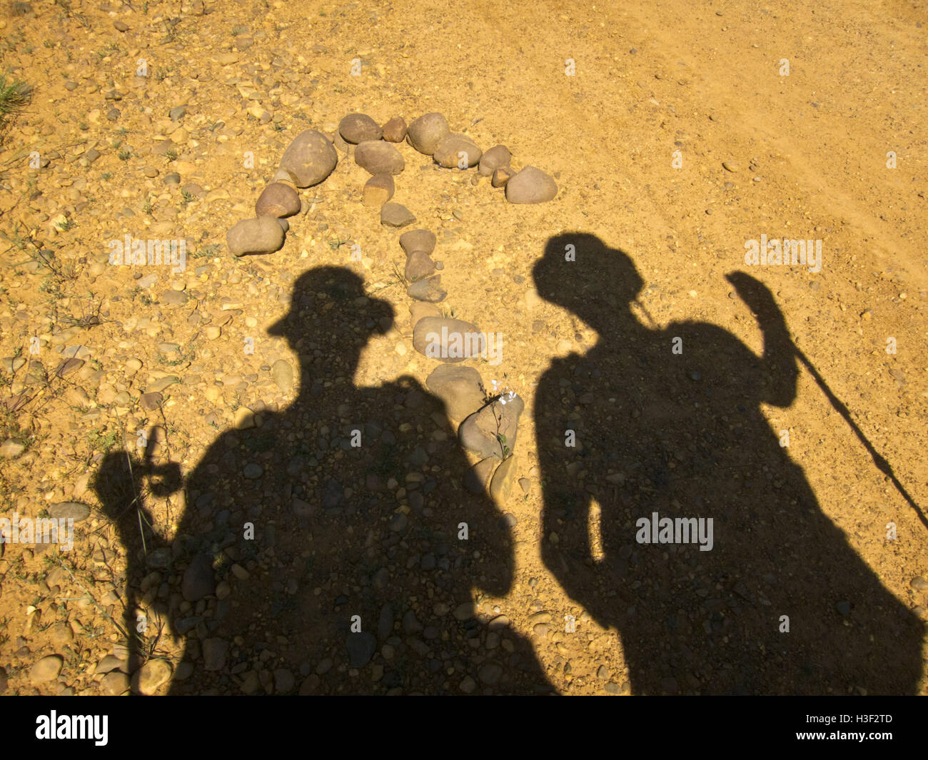 Shadows of two pilgrims standing over stone arrow along the Camino de ...