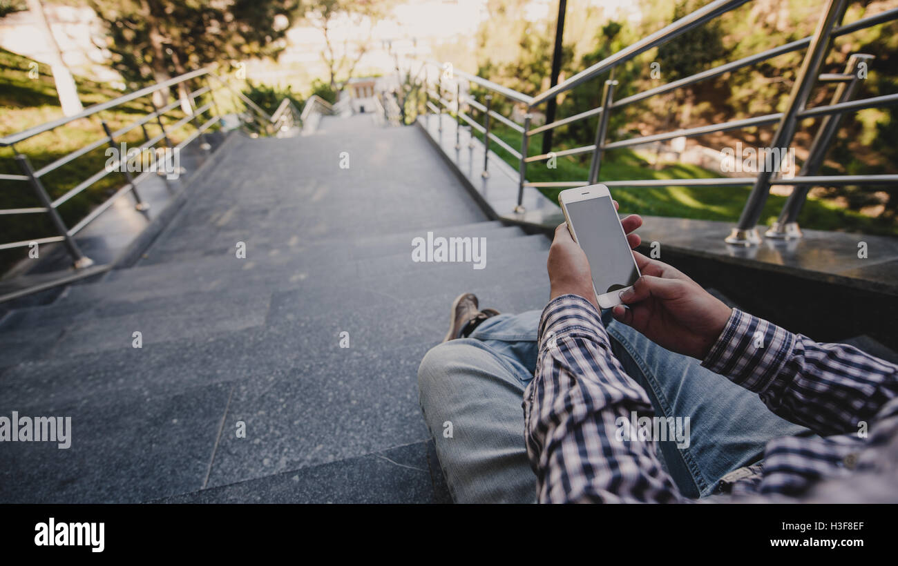 young Man with the phone in his hand sitting on the steps. top view ...