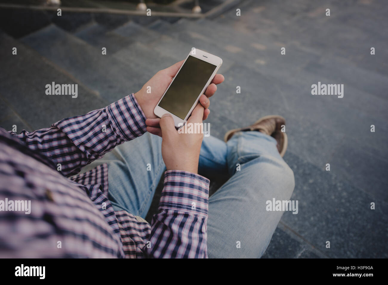 young Man with the phone in his hand sitting on the steps. top view ...