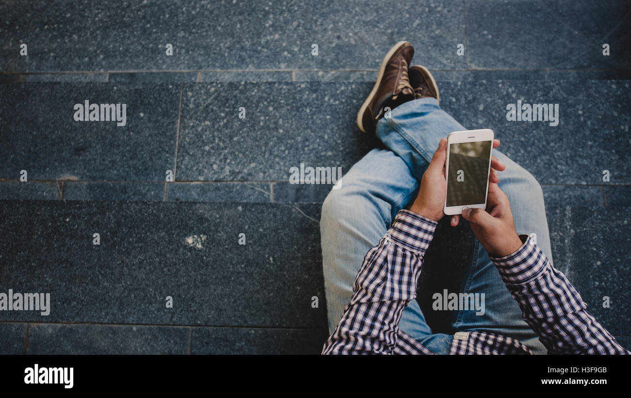 young Man with the phone in his hand sitting on the steps. top view ...
