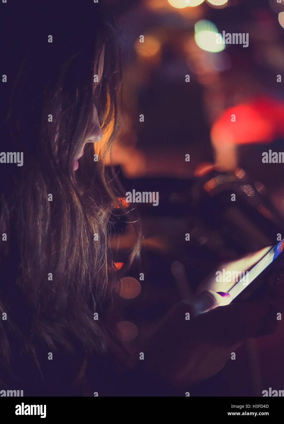 Girl using smart phone at night in front of blurred city lights Stock ...