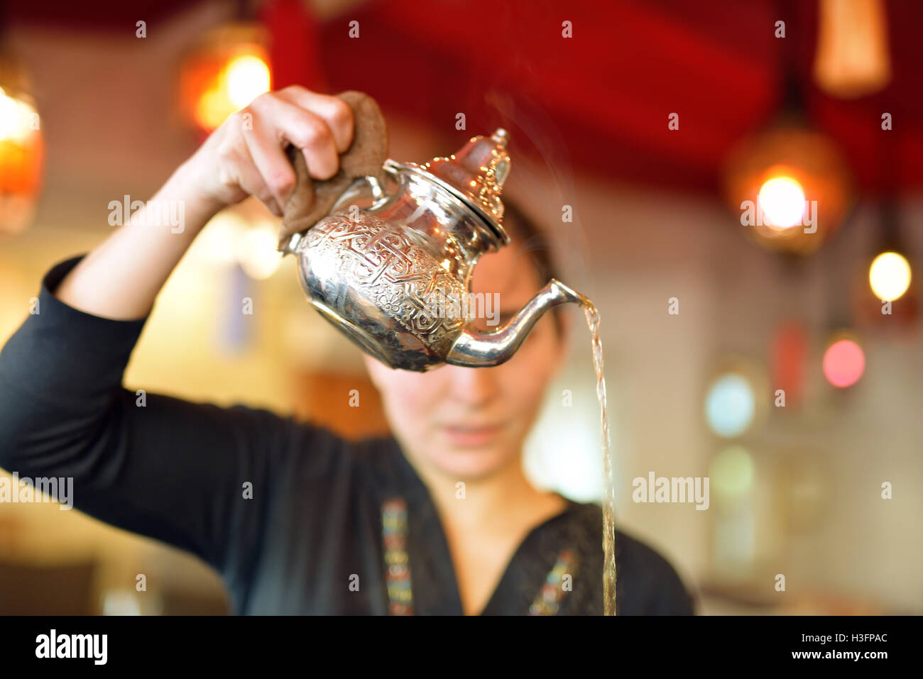 A girl (waitress) serves Indian tea in a restaurant with colorful lamps ...