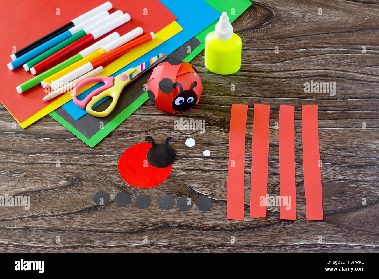 The child makes crafts out of paper ladybug. Glue, paper, scissors on a ...