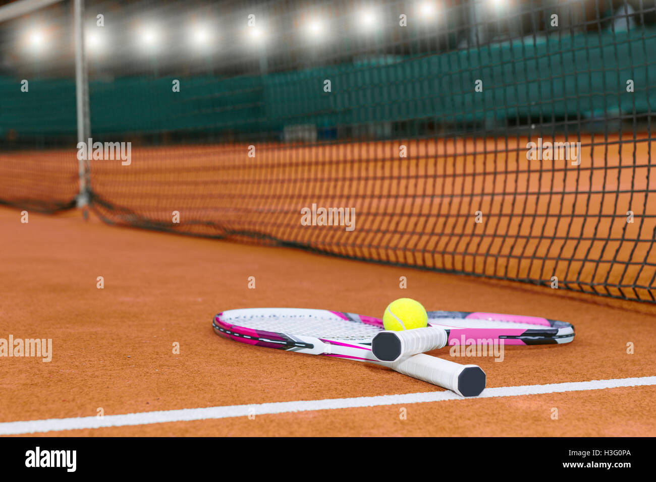 Two tennis rackets with a tennis ball lying near net on clay court ...