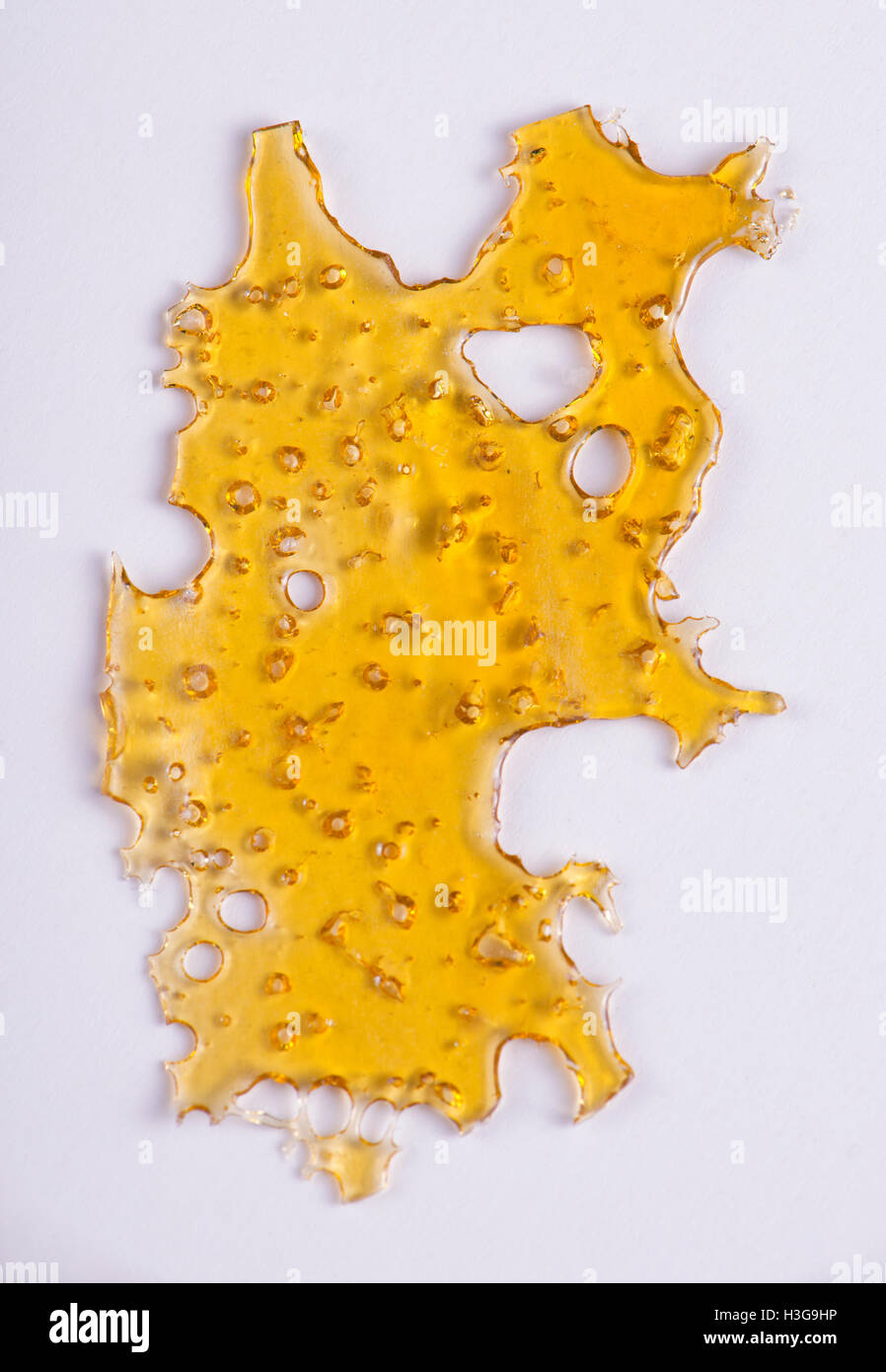 A piece of cannabis oil concentrate aka shatter isolated against white ...