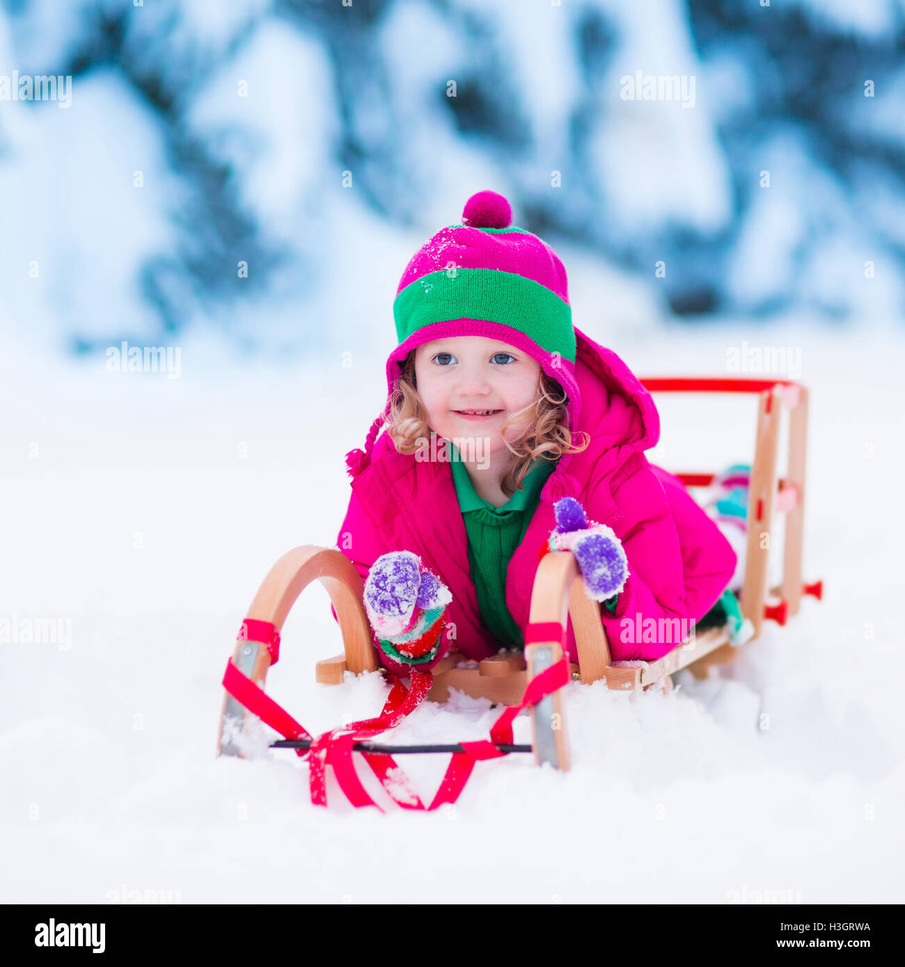 Little girl enjoying a sleigh ride. Child sledding. Toddler kid riding a sledge. Children play ...