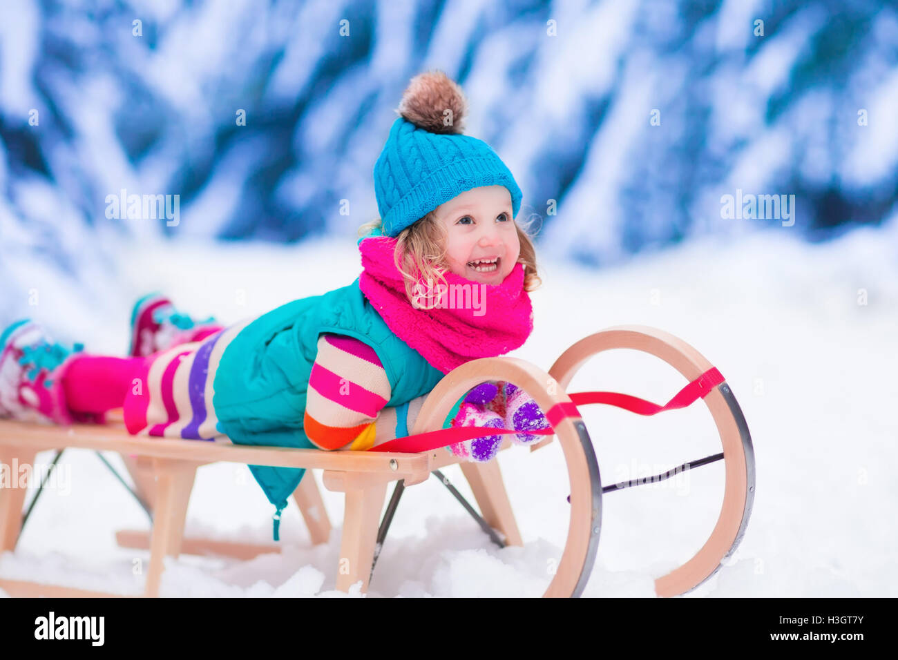 Little girl enjoying a sleigh ride. Child sledding. Toddler kid riding a sledge. Children play ...