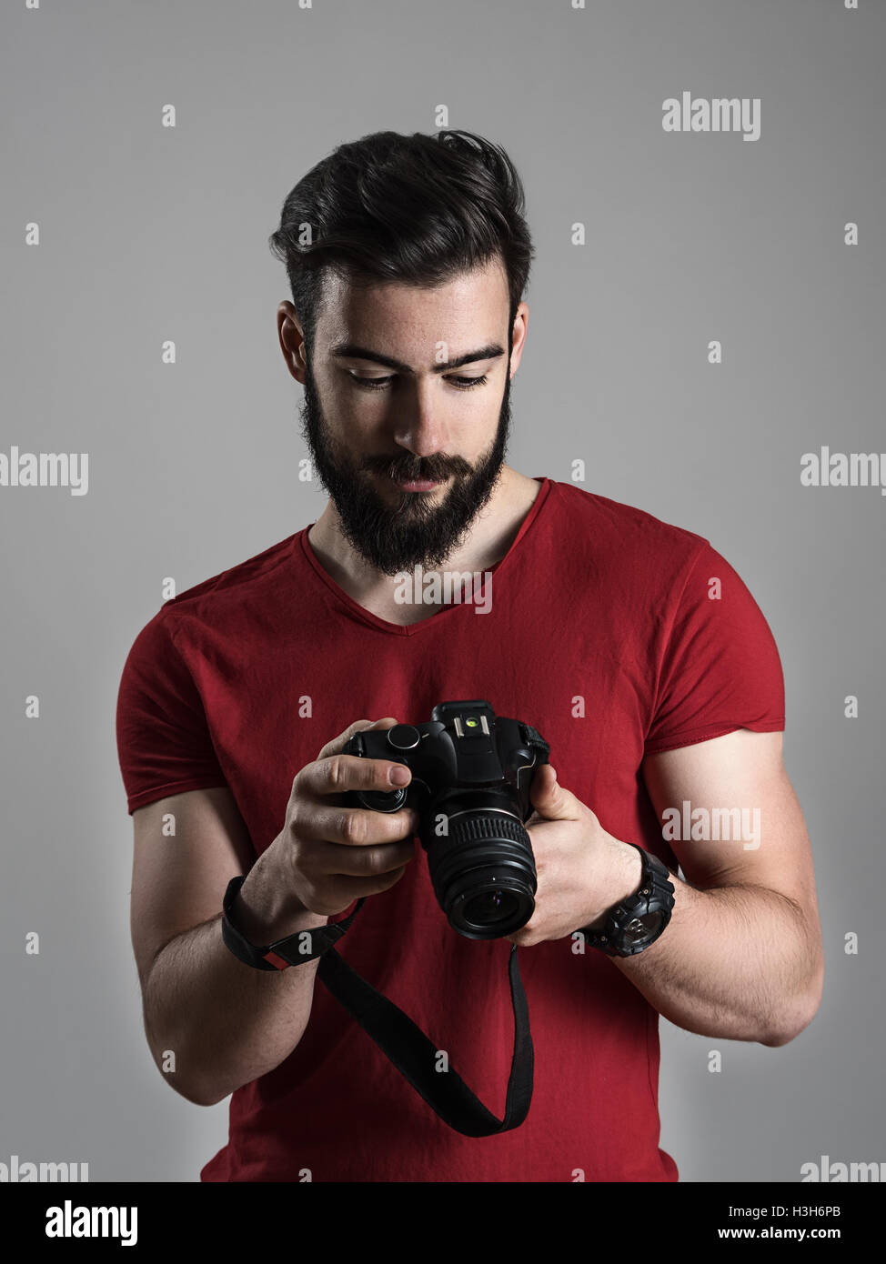 Young bearded photographer reviewing photos on rear lcd screen of dslr ...