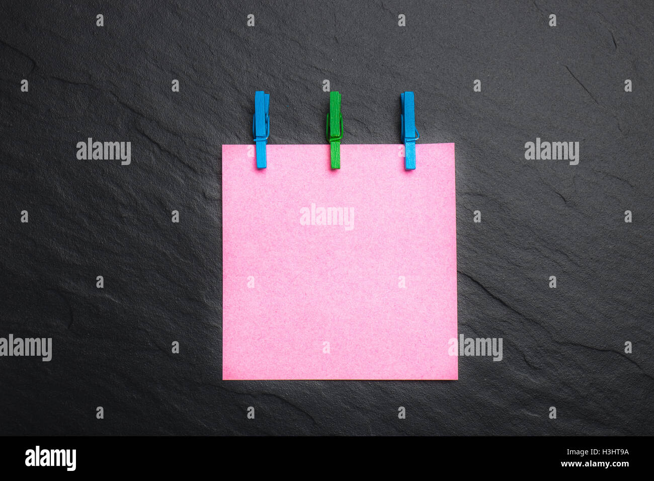 close up of a pink note paper and clothes pegs on a black background ...