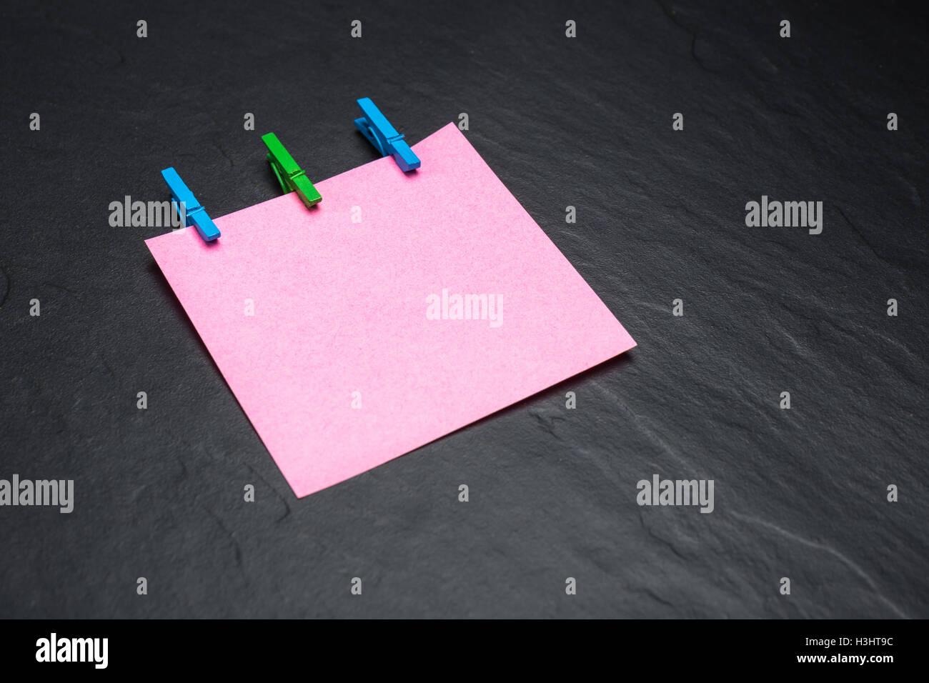 close up of a pink note paper and clothes pegs on a black background ...