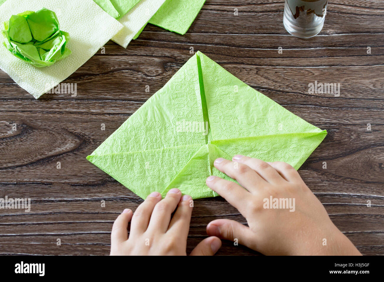 The child holds a paper square and fold it corner. The child makes ...