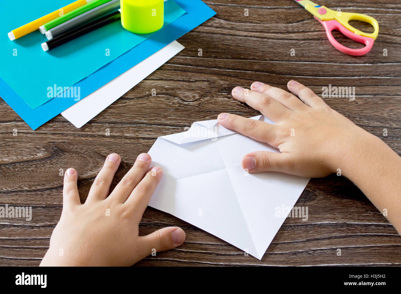 The child holds a paper strip square and fold it corner. The child ...