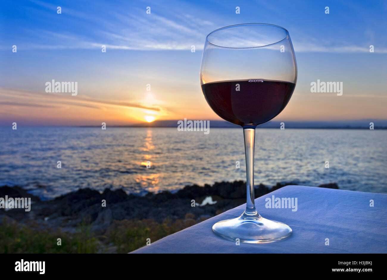 SUNSET RED WINE COAST SEA LANDSCAPE Glass of red wine on alfresco ...