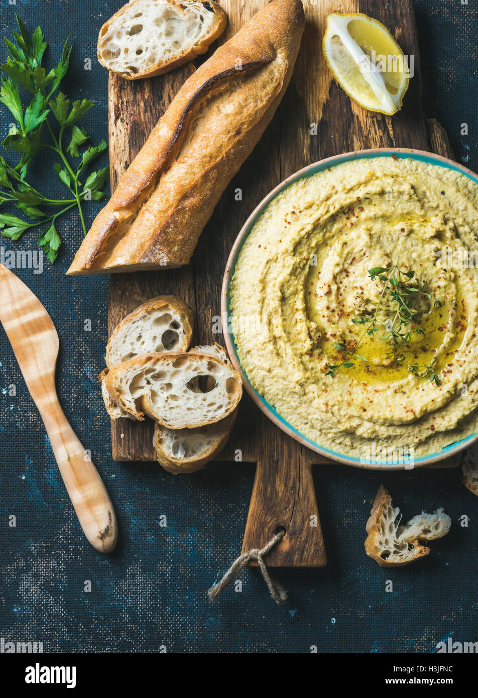 Homemade hummus with lemon, herbs and baguette on rustic wooden serving ...