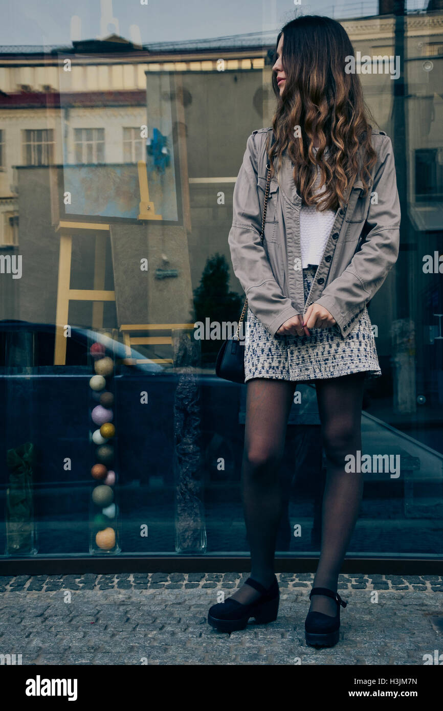 Stylish girl in skirt standing near glass shop window on city street ...