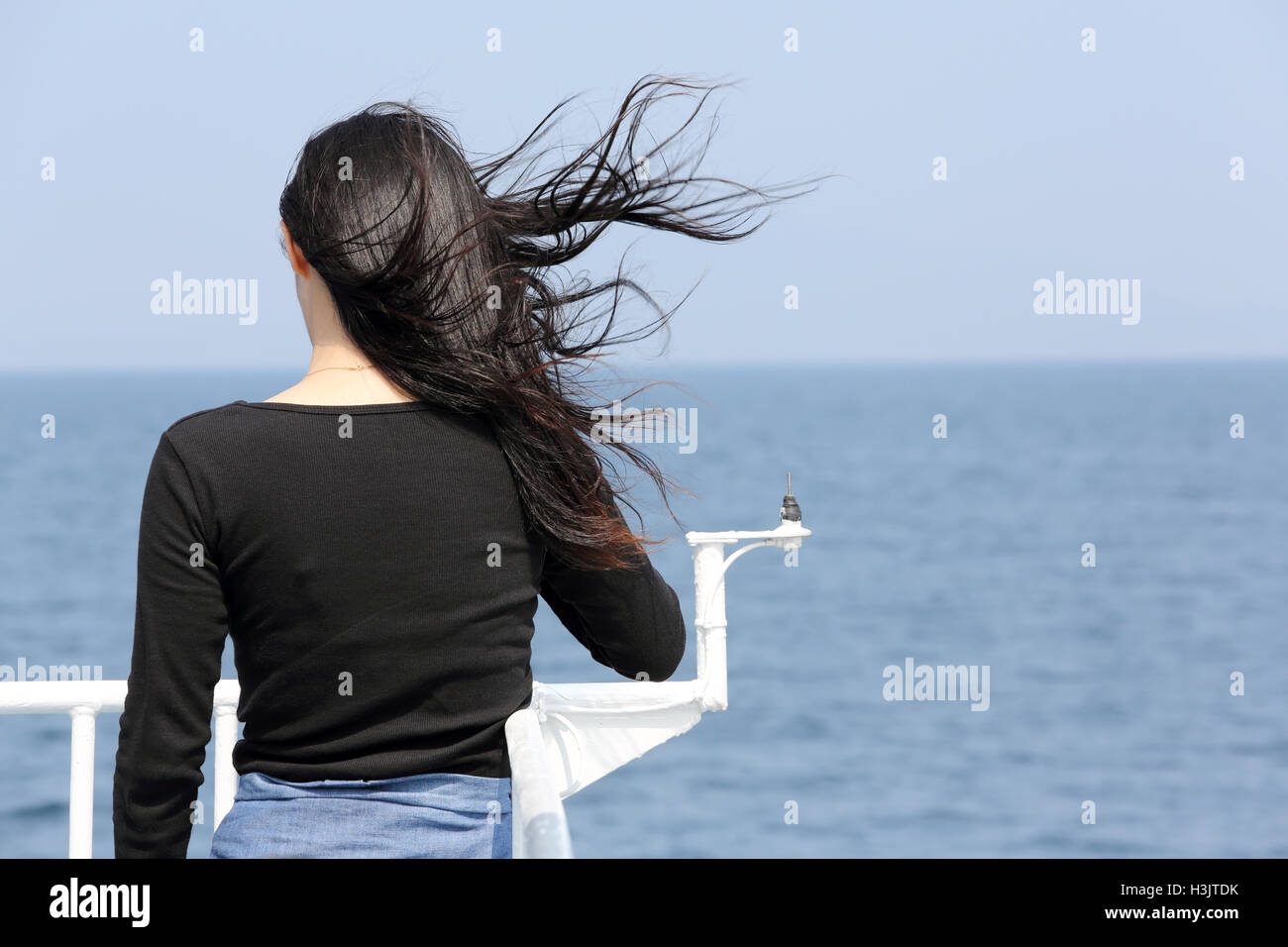 Back view of young asian woman with waving long hair looking at the sea ...