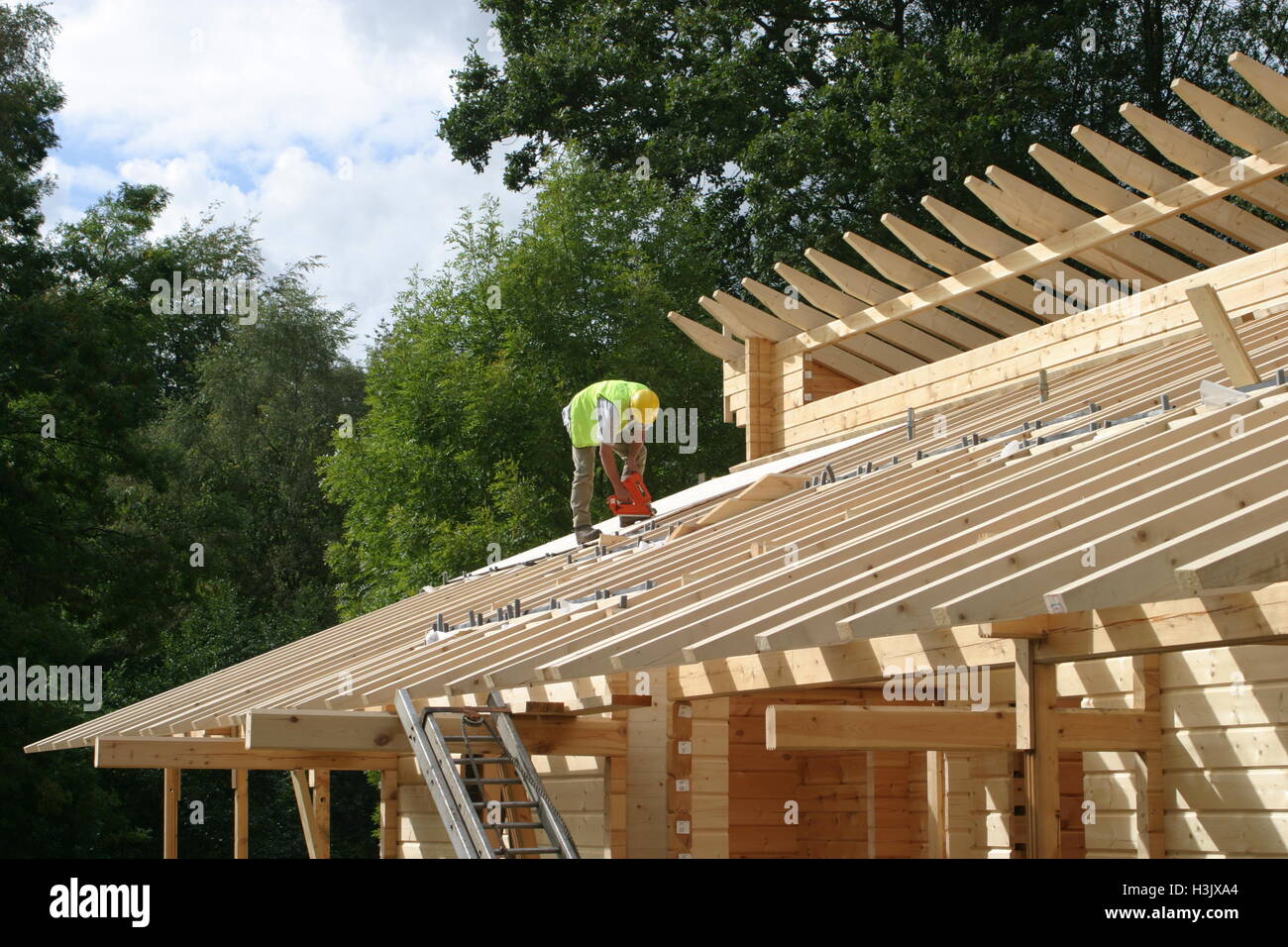 A worker uses a gas-powered nail gun to fasten roofing boards on a ...