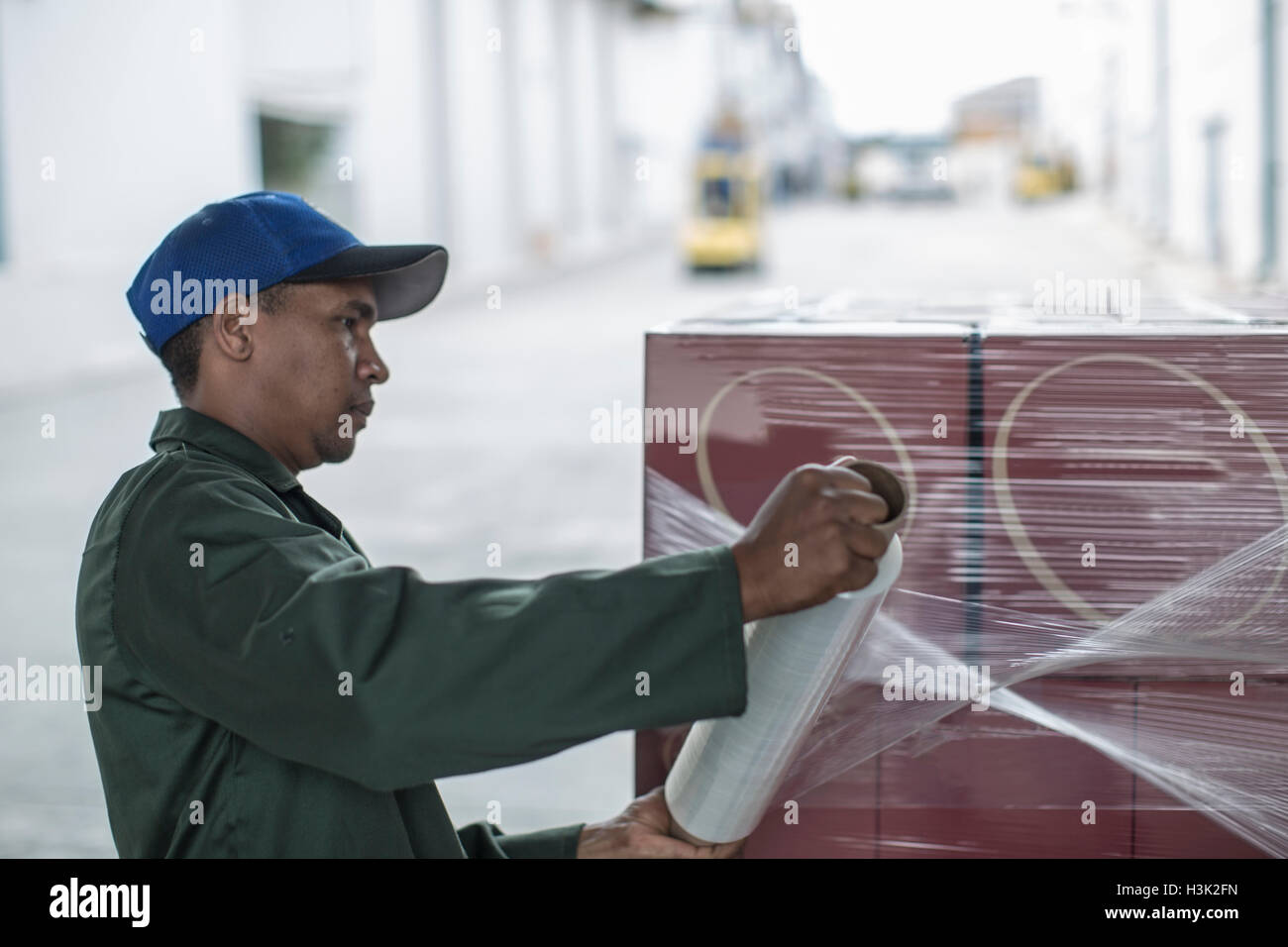 Factory worker wrapping pallet in plastic wrap at packaging factory ...