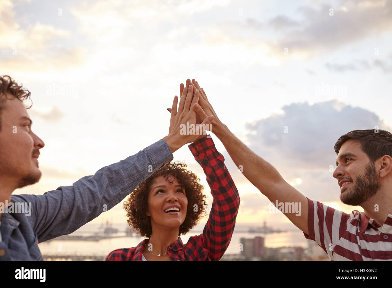 Three happy, smiling friends doing a high five with a city scape behind ...