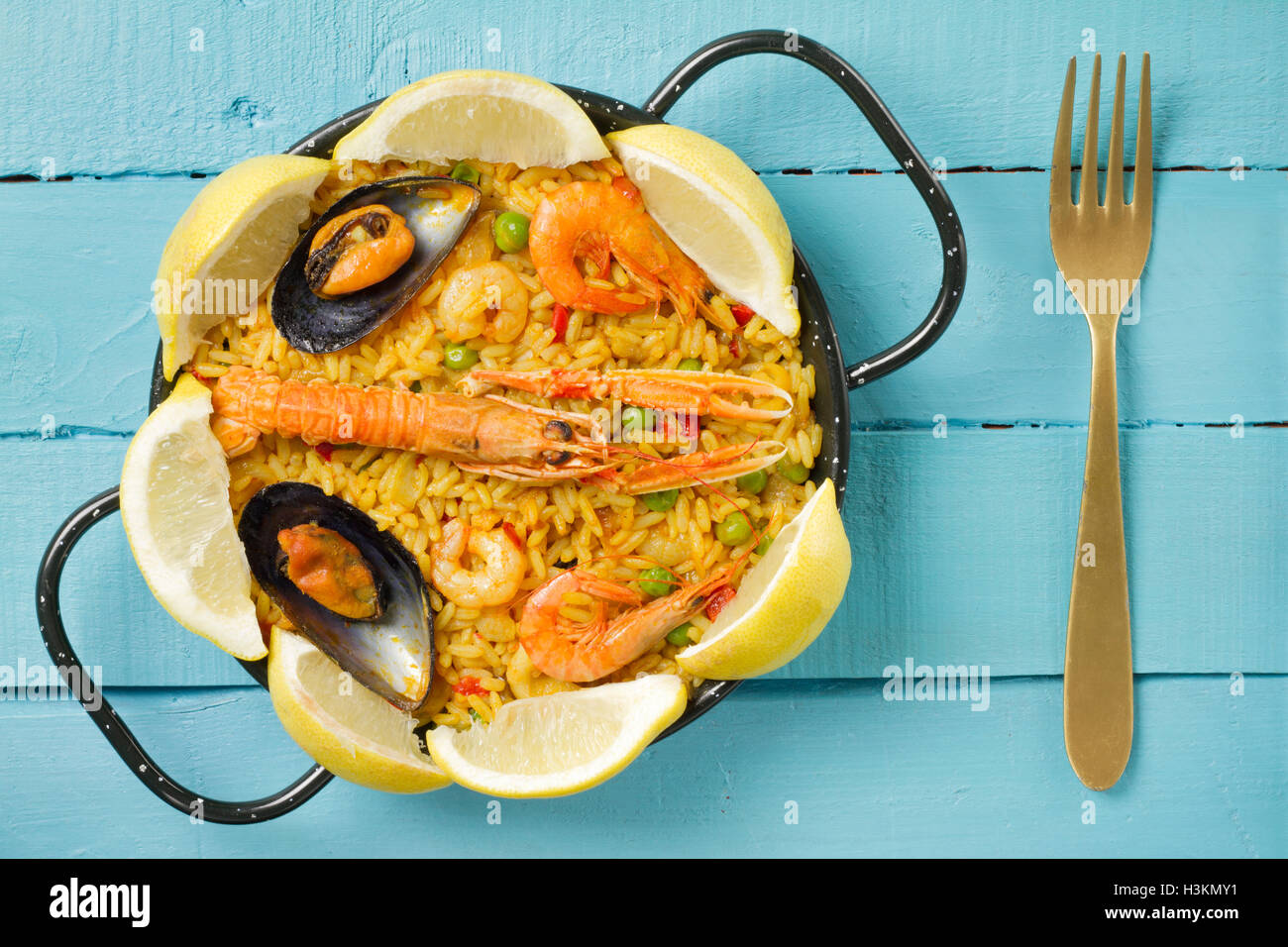 Spanish paella on a blue wooden table with fresh lemon and a golden ...